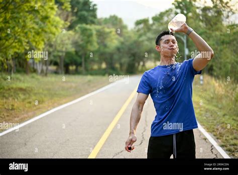 tired and exhausted millennial asian male runner pouring water from a