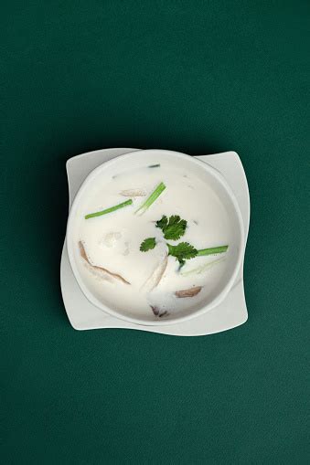 크림 같은 육수에 닭고기와 허브를 곁들인 태국 코코넛 수프 한 그릇 톰 카 가이의 모습은 녹색 배경에 흰색 세라믹 그릇에 담겨 정통 태국 요리를 제공합니다 0명에 대한 스톡