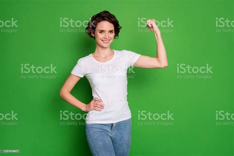 매력적인 자신감 레이디 물결 모양의 머리를 흔들어 완벽한 모양 이두근 팔 승리 경쟁을 착용 캐주얼 흰색 티셔츠 청바지 고립 밝은 녹색 색상 배경의 사진 한 명의 여자만에