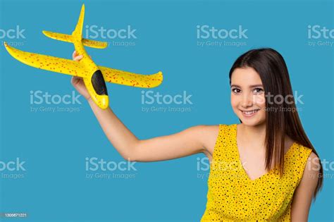 고립된 파란색 배경 위에 조명색 비행기 장난감을 들고 있는 젊은 사업가가 이빨을 보여주는 자신감 넘치는 미소에 만족합니다 항공기 모델을 검사하는 백인 여성 파트너 개념에