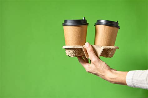 검은 색 뚜껑이있는 두 컵 갈색 종이를 들고 있는 손 2 개의 커피 특별 제안 또는 프로모션 녹색 배경에 두 컵을 들고 손 차 나 커피 갈 수 있습니다 검은 뚜껑이 달린