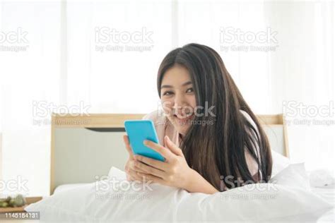 분홍색 잠 옷에 있는 웃는 여자의 초상화 휴대 전화에서 정보 보기 침대에 아침 빛을 환영 합니다 귀여운에 대한 스톡 사진 및 기타 이미지 Istock