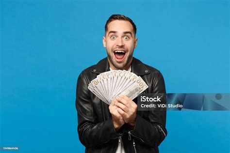 블랙 가죽 자 켓 흰색 T 셔츠에 젊은 이루어지지 남자는 현금 돈의 팬을 잡고 파란색 벽 배경 스튜디오 초상화에 고립 된 달러 지폐 사람들 라이프 스타일 개념입니다 복사