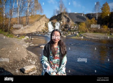 Yakut Asian Girl In Glasses Posing Smiling On The Background Of A Small Waterfall In The Fall