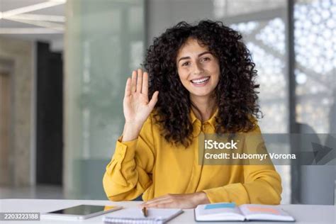 직장 사무실 안에 앉아 카메라를 바라보며 손을 흔들며 인사를 건네고 온라인 회의 비즈니스 미팅에서 동료들과 이야기를 나누는 여성 25 29세에 대한 스톡 사진 및 기타