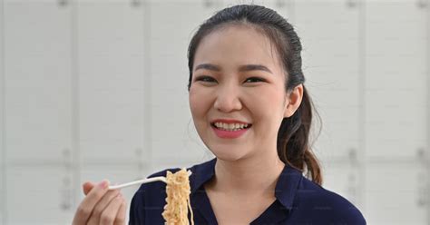 웃고 있는 아시아 여자는 사무실에서 인스턴트 국수를 먹는 플라스틱 포크를 들고 있다 사진 Unsplash의 라면 제품 이미지