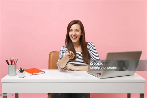 카메라에 여자 포인팅 연필 파스텔 핑크 배경에 고립의 현대 Pc 노트북과 흰색 책상에서 작업을 앉아 행복 하 게 웃 고 있다 성과 비즈니스 경력 개념입니다 광고에 대 한