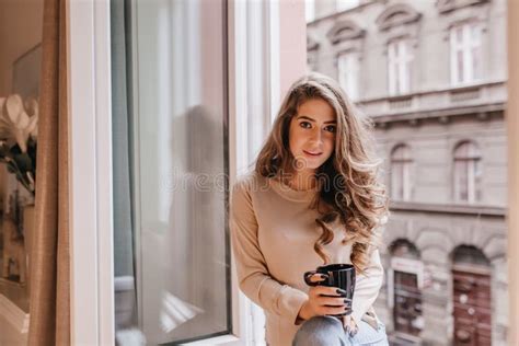Interested Shy Girl With Long Hair Posing With Cup Of Tea On Sill Indoor Portrait Of Good