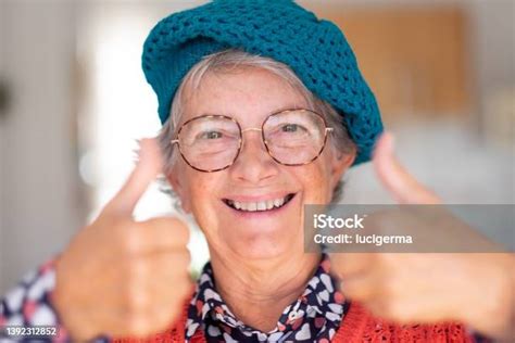 모자와 안경을 쓰고 카메라를 바라보는 손으로 긍정적 인 신호를 몸짓하는 매력적인 시니어 여성의 초상화 70 79세에 대한 스톡 사진 및 기타 이미지 Istock