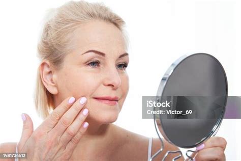 거울을 보고 얼굴 피부를 만지는 행복한 중년 여성 모델 건강한 피부 관리 노화 아름다움 스킨케어 치료 화장품 개념을 즐기는 웃고 있는 성숙한 나이든 아가씨 50 54세에
