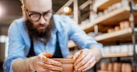 앞치마를 입은 도공 노동자로 잘 생긴 남자가 작은 제조업에서 도자기 바퀴에 점토 주전자를 만드는 사진 Unsplash의 도공 이미지