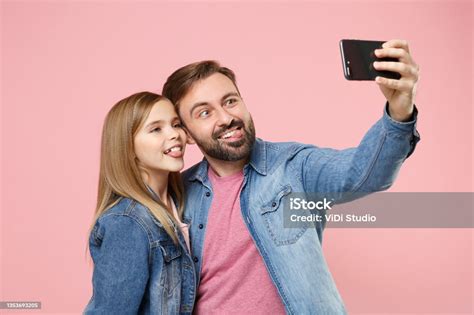 쾌활한 수염을 기고한 남자 와 아이 아기 소녀 파스텔 핑크 배경에 고립 된 아버지 의 작은 아이 딸 가족 부모 어린 시절 개념을 사랑해요 혀를 보여주는 휴대 전화에 셀카