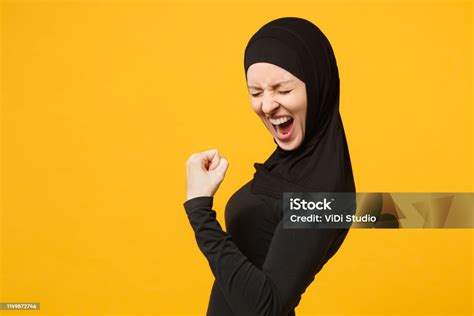 과다 한 젊은 아라비아 무슬림 여 자가 히 잡 검은 옷을 하 고 위 너 제스처를 하 고 예 노란 벽 배경 스튜디오 초상화에 고립