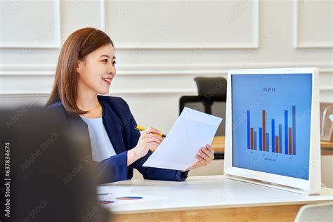 비즈니스우먼 회사 업무 근무 사무실 모니터 앞에 앉아 서류 보며 업무을 보고 있는 직장인 모습 Stock 写真 Adobe Stock