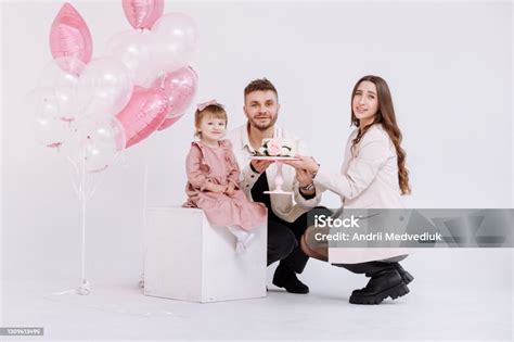 젊은 부모 엄마와 아빠는 생일을 축하하고 있다 그들의 두 살 짜리 아이 가족의 빛과 분홍색 공생일 장식의 배경에 꽃과 케이크에 촛불을 불고 18 23 개월에 대한 스톡 사진