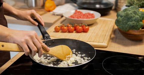 부엌에서 전기 스토브 옆에 서 있는 동안 프라이팬에 다진 양파를 섞는 젊은 여자의 손 사진 Unsplash의 튀기다 이미지