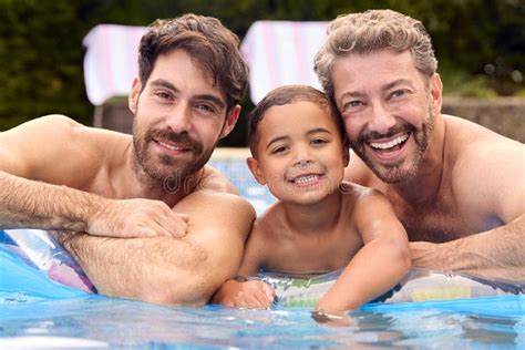 Portrait Of Same Sex Family With Two Dads And Son On Holiday In Swimming Pool Together Stock