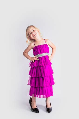 파란 복고풍 드레스와 어머니의 특허 가죽 하이힐 신발을 입고 웃는 얼굴로 놀라운 소녀가 위를 쳐다 봅니다 회색 배경에서