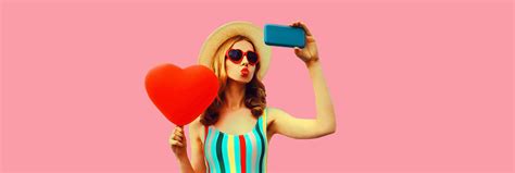 밀짚 모자 분홍색 배경에 선글라스 광고 텍스트를 위한 빈 복사 공간을 착용한 빨간 하트 모양의 풍선으로 스마트폰으로 셀카를 찍는 아름다운 젊은 여성의 여름 초상화 25 29