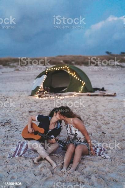 해변에 텐트 근처의 석양에 기타를 연주하는 젊은 성인 커플 여자 동성애자에 대한 스톡 사진 및 기타 이미지 여자 동성애자 커플 기타 현악기 Istock