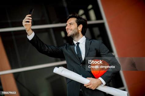 전화를 사용하여 프로젝트와 하드 모자를 가진 젊은 건설 엔지니어 남자 건물 외관에 대한 스톡 사진 및 기타 이미지 건물 외관