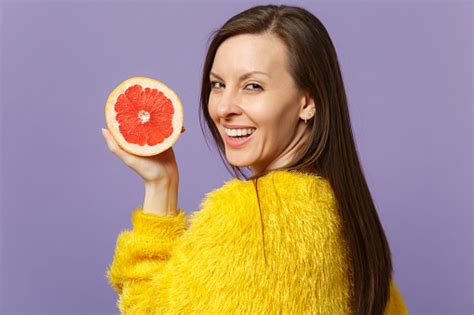 스튜디오에서 보라색 파스텔 배경에 고립 된 신선한 잘 익은 자 몽의 절반을 들고 모피 스웨터에 쾌활 한 젊은 여자 사람들은 생생한 라이프 스타일 휴식 휴가 개념입니다 복사