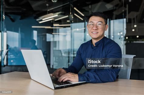 현대 사무실 건물 내부의 노트북에서 일하는 안경을 쓴 젊고 성공적인 아시아 사업가 웃고 카메라를보고있는 행복한 관리자 기업가 투자자 초상화 사무실에 대한 스톡 사진 및 기타