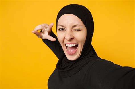 가까이에 젊은 아라비아 무슬림 여자 히 잡 블랙 옷 노란 벽 배경 스튜디오 초상화에 고립 된 휴대 전화에 Selfie 샷을 하 고 사람들 종교적 라이프 스타일 개념입니다