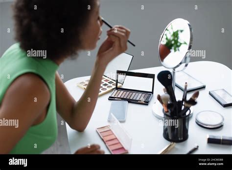 Side View Of Blurred African American Woman Applying Cosmetics Near Cellphone With Blank Screen