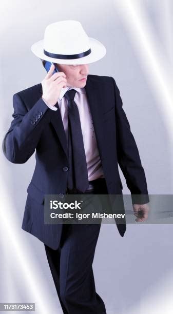성공으로 가는 길에 비즈니스 라이프 양복을 입고 흰색 모자와 선글라스를 입고 스마트폰으로 이야기하고 하얀 배경을 걷고 있는 의도적인 매력적인 사업가 걷기에 대한 스톡 사진