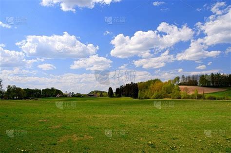 一片广阔的田野或草地，远处有一座被树木覆盖的高山，以及在波兰乡间多云的春天天空下的一些耕过的田地