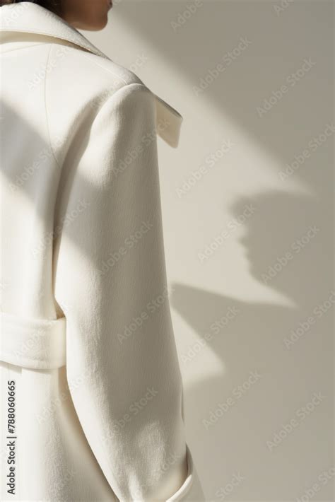 옆모습의 여성 모델 미니멀리스트 화이트 코트 낮은 디테일과 깔끔한 라인 베이지 색상 오버사이즈 룩북 사진 초미세 디테일 그늘진 허리 건장한 어깨의 옆모습