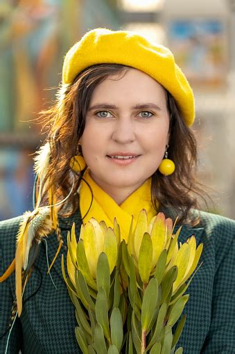 녹색 바지 수트와 노란 베레모를 쓴 젊은 여성이 미술관을 배경으로 노란 봄 꽃 꽃다발을 들고 서 있습니다 봄 휴가의 개념 3 월 8 일 부활절 3월에 대한 스톡 사진 및