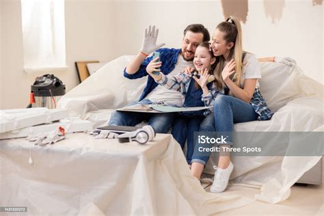 데님 스타일의 옷을 입은 가족이 개조 공사중인 아파트의 소파에 앉아 있습니다 갈색 머리 딸은 어머니의 전화를 가져 와서 행복한 가족 셀카를 기억으로 삼았습니다 3 명에 대한