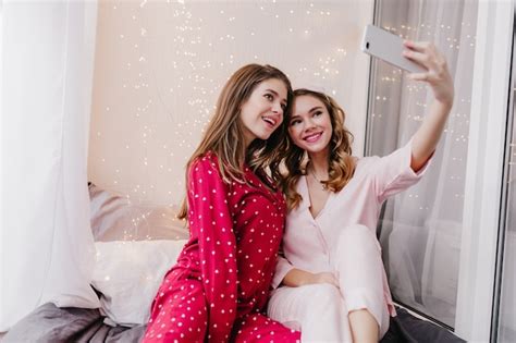 Симпатичные девушки сидят на кровати и позируют для селфи Фотография в