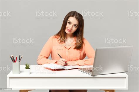 파스텔 캐주얼에 젊은 매력적인 여자 메모를 쓰고 앉아서 회색 배경에 고립 된 Pc 노트북으로 흰색 책상에서 일 합니다 성취 비즈니스 커리어 라이프 스타일 컨셉 복사 공간을
