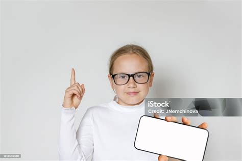 흰색 배경에 스마트 폰을 가리키는 사랑스러운 어린이 소녀 아이는 새로운 응용 프로그램 또는 모바일 웹 사이트 모형 배너에 대 한 큰 빈 빈 흰색 화면 디스플레이와 휴대