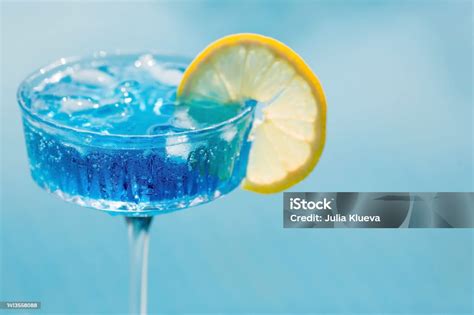 수영장 배경에 맛있는 파란색 칵테일 블루 라군과 노란색 레몬 한 잔 알콜 칵테일 육즙이 많은 과일 블루와 Curacao 리큐어 아이스 큐브 및 레몬 조각 0명에 대한 스톡