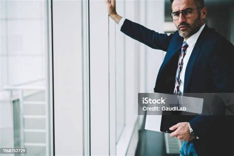 현대 의 태블릿 장치를 손에 들고 카메라를 보고 자신감 성공적인 사업가 50 세의 절반 길이 초상화 정장 옷을 입고 금융 회사의 심각한 성숙한 소유자 50 54세에 대한