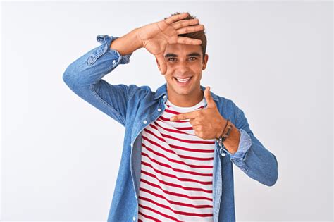 스트라이프 티셔츠와 데님 셔츠를 입은 젊은 잘생긴 남자는 고립 된 흰색 배경 위에 행복한 얼굴로 손과 손가락으로 프레임을 만드는 미소 창의력과 사진 개념 T 셔츠에 대한