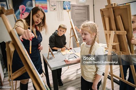 교사가 미술 수업에서 아이들에게 그림 그리는 방법을 설명합니다 미술 수업에서 붓과 이젤을 든 한 무리의 학생들이 풍경을 그리기 시작했습니다 아이들은 공방에서 그림 그리기를