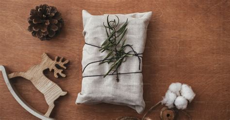 세련 된 크리스마스 소박한 선물은 소나무 콘 순록 꼬기 면화가있는 나무 테이블에 녹색 가지가 있는 린넨 패브릭으로 싸여 있습니다 플랫 레이 심플한 에코는 플라스틱을