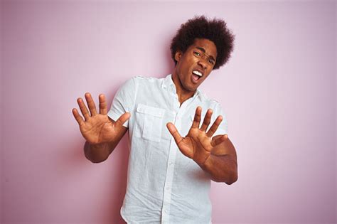 고립된 분홍색 배경 위에 서있는 흰색 셔츠를 입은 젊은 미국 남자는 두려움 표정으로 두려워하고 손으로 제스처를 멈추고 충격에 고함을 쳤습니다 공황 개념 개념에 대한 스톡