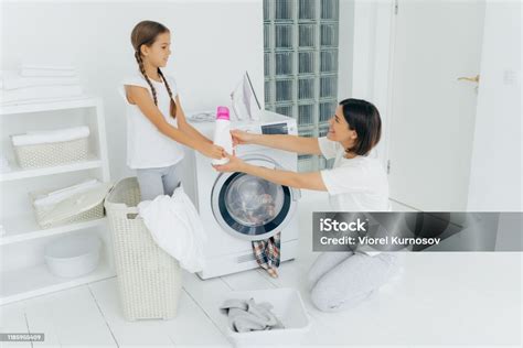 사랑스러운 소녀는 세탁과 엄마를 도와 바구니에 서 세제 또는 세척 분말의 병을 제공합니다 여자는 무릎에 서 세탁기를 로드 하는 딸의 도움을 받을 행복 세탁기세탁기세탁기를