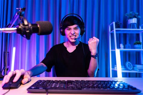 스마트 폰에서 비디오 게임을합니다 손에 핸드폰을 들고 의자에 앉아있는 젊은 아시아 잘 생긴 남자 네온 룸에서 온라인 모바일 게임에서 헤드셋을 착용 스트리머를 종료했습니다