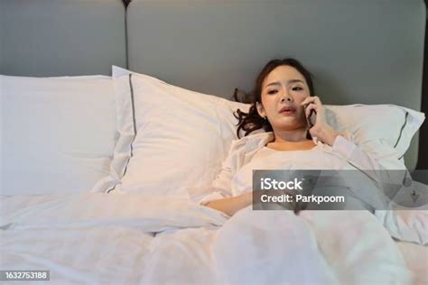 하얀 잠옷을 입은 젊고 아름다운 아시아 여성이 잠자리에 들기 전에 모바일 스마트폰이 있는 침실에 누워 좋은 꿈을 꾸고 있다 라이프스타일 컨셉 취침시간에 대한 스톡 사진 및