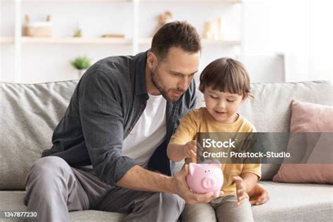조기 금융 교육 귀여운 어린 소년 돼지 저금통에 동전을 넣어 아빠는 유지하고 안전한 돈을 자신의 아들을 가르치는 돼지 저금통에