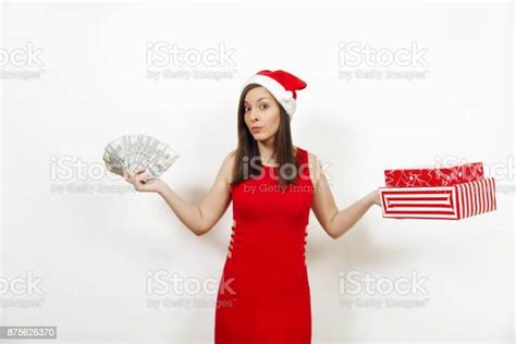 젊은 Disconfused 빨간 드레스와 크리스마스 모자 흰색 배경에 선물 상자와 돈 지폐를 들고 좌절된 여자 현재와 산타 소녀와 격리 하는 현금입니다 새 해 휴일 2018
