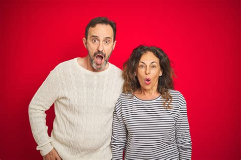 고립 된 빨간 배경 에 겨울 스웨터를 입고 아름다운 중년 부부는 놀라움의 표정 두려움과 흥분 된 얼굴로 충격을 받았습니다 놀라움에 대한 스톡 사진 및 기타 이미지 Istock