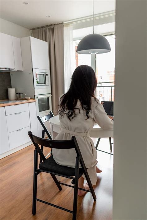 Young Woman In Comfortable White Robe Works On Laptop While Sitting At